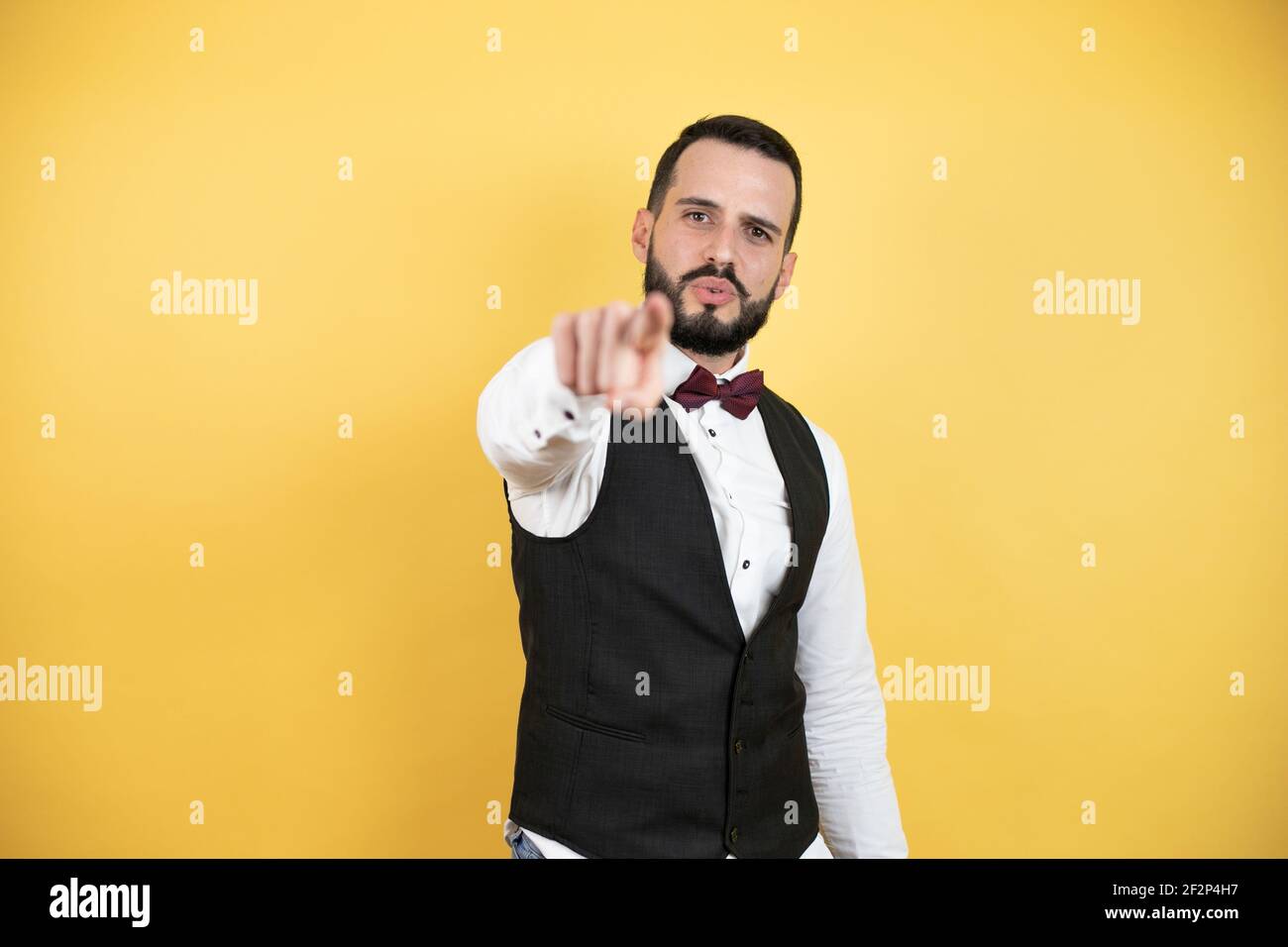 Young man with beard wearing bow tie and vest pointing with finger to ...