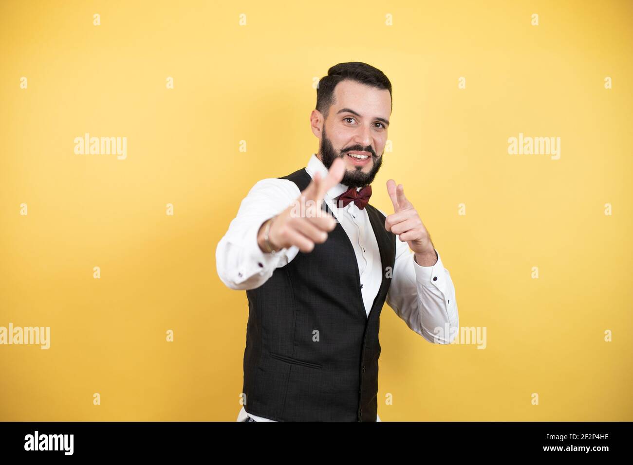 Young man with beard wearing bow tie and vest pointing to you and the ...