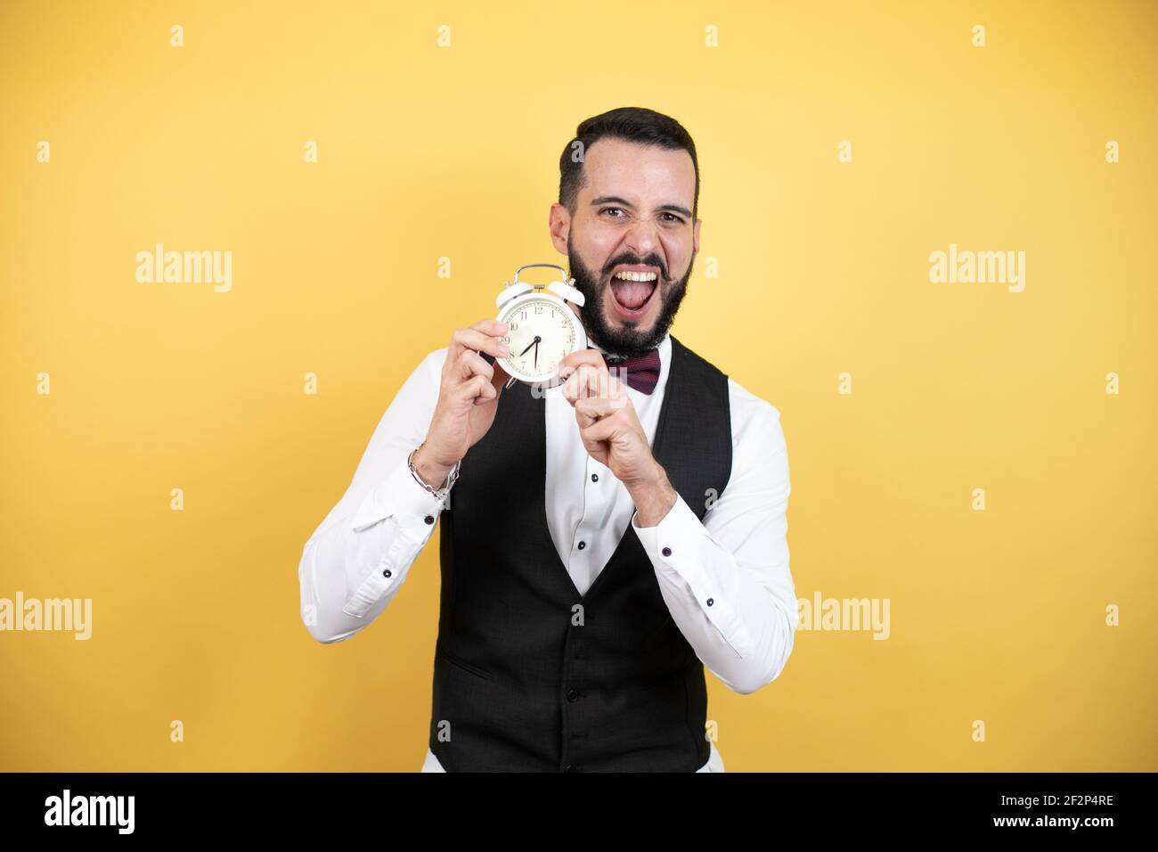 Young man with beard wearing bow tie and vest screaming and scared ...