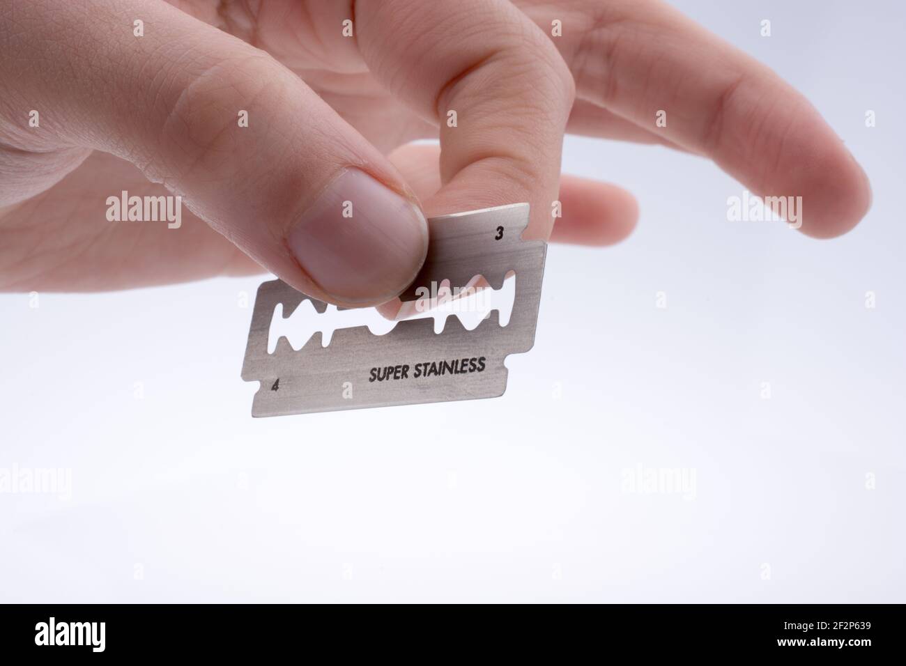 Hand holding a razor blade on a white background Stock Photo - Alamy