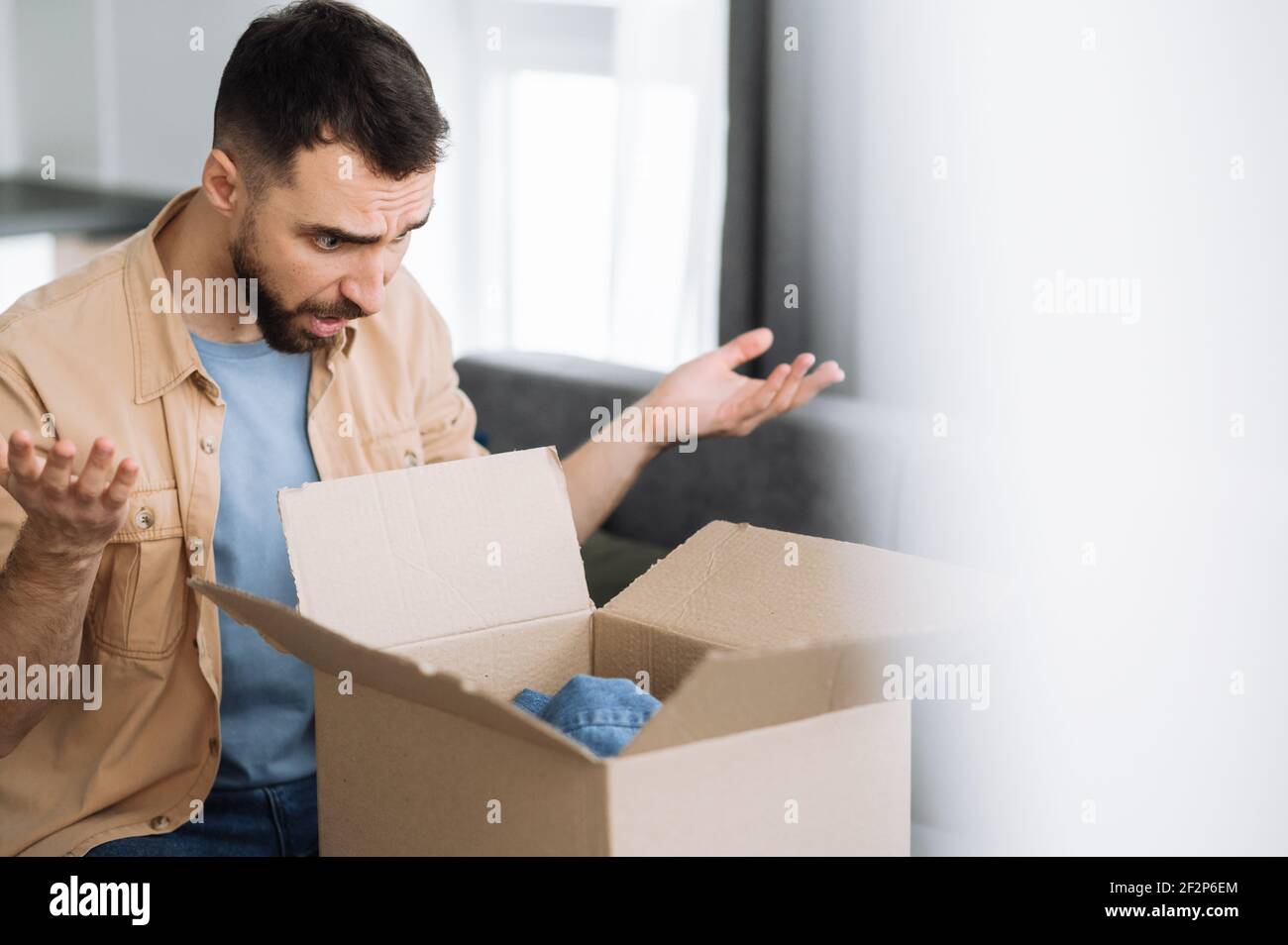 Home delivery. Confused young man sits on the couch, unpacking his ...