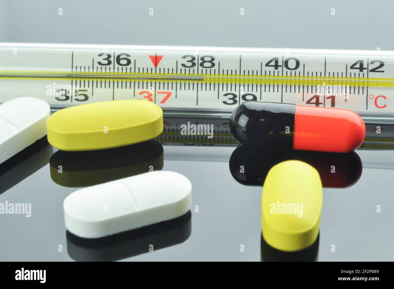 Mercury thermometer and different pills and capsule on a glossy black ...
