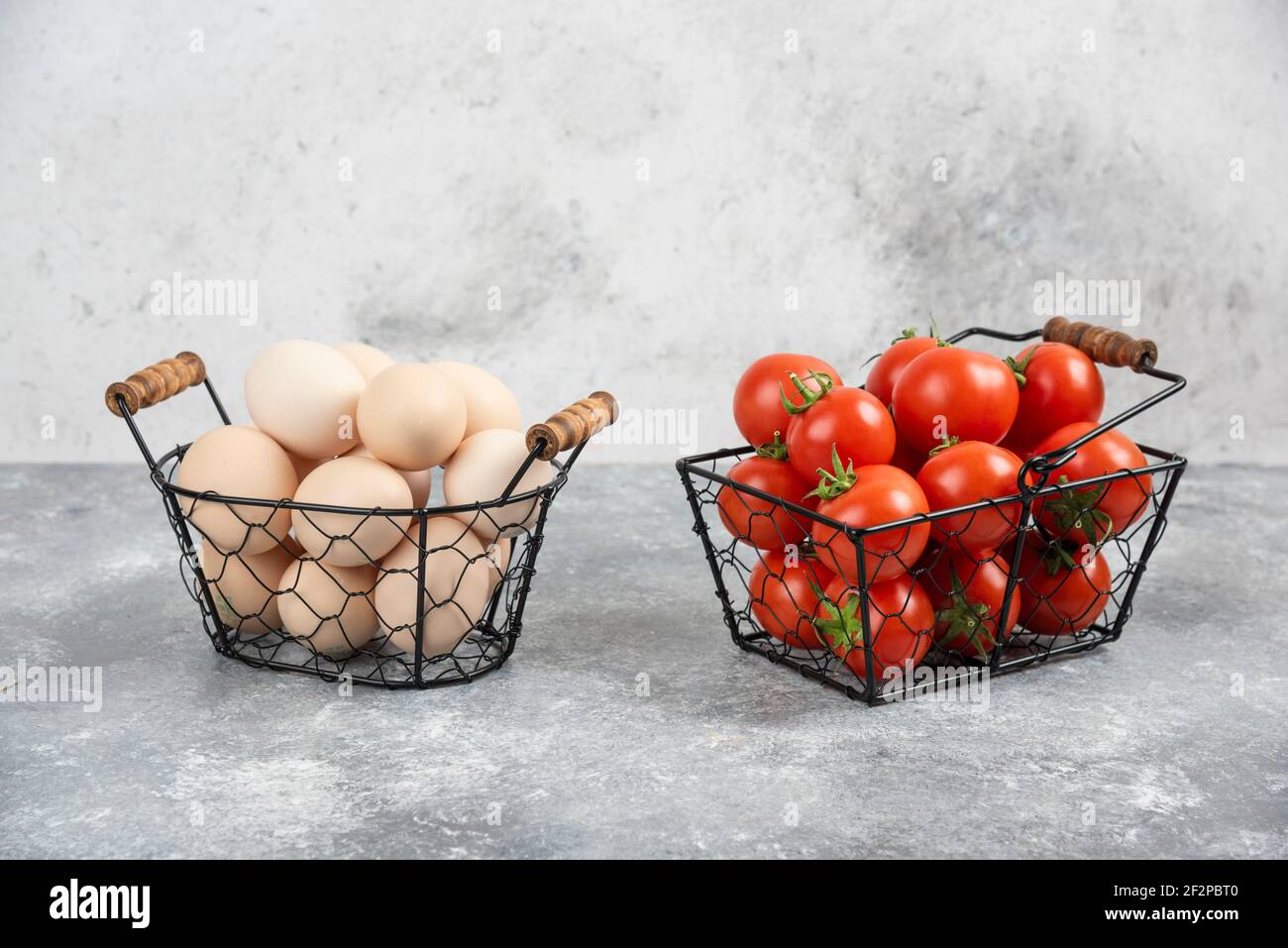 Wicker basket of raw organic eggs and red tomatoes on marble background ...