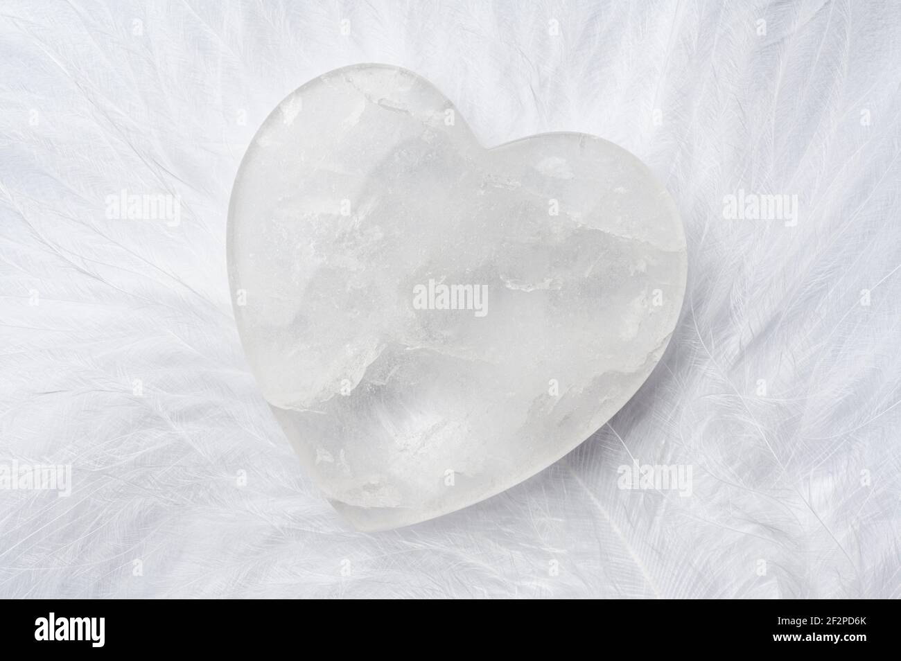 Rock crystal heart on white down feather, symbol of purity, innocence ...