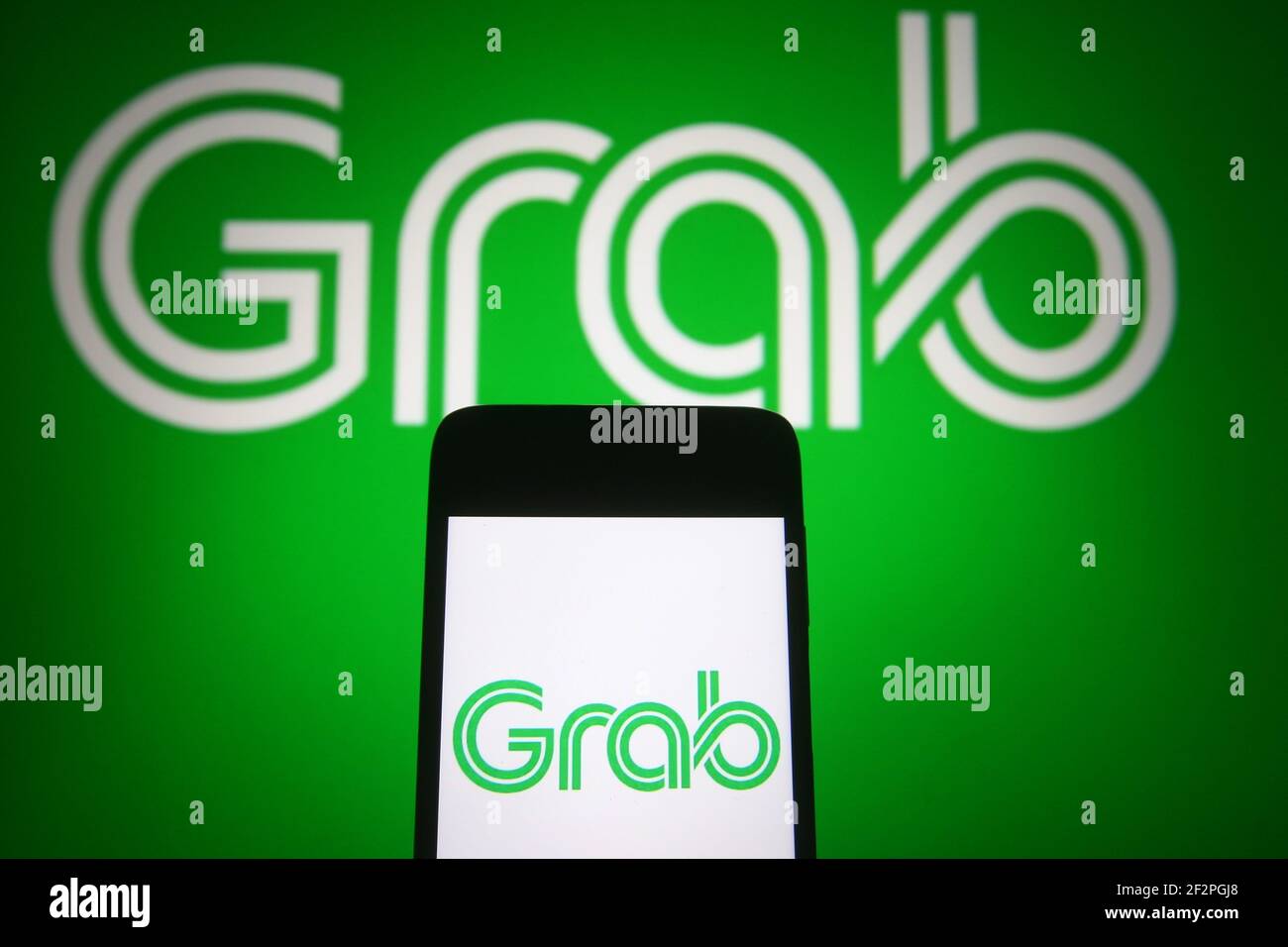 In this photo illustration a Grab logo is seen on a smartphone and a pc ...