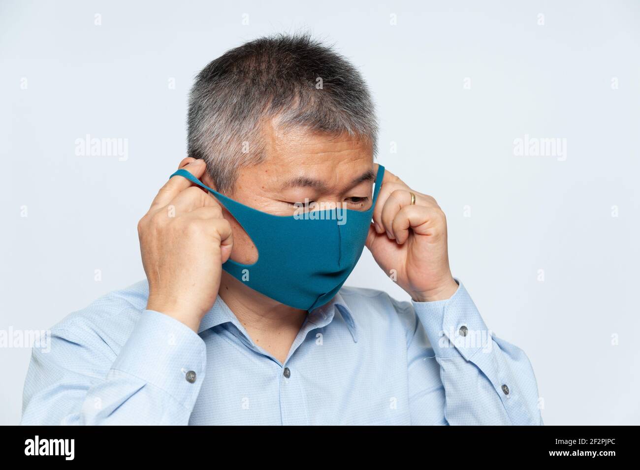 Middle-aged Asian man putting on a reusable polyurethane face mask to ...