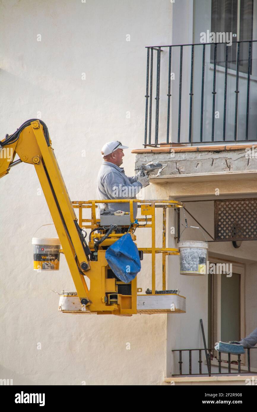 Spanish builder repairing a balcony whilst standing on a cherry picker ...