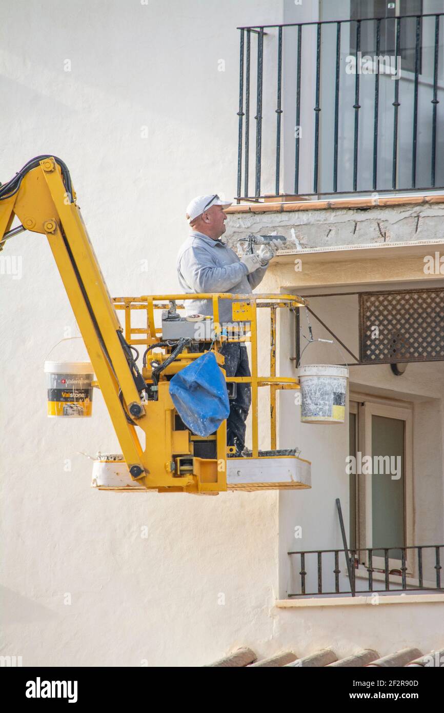 Spanish builder repairing a balcony whilst standing on a cherry picker ...