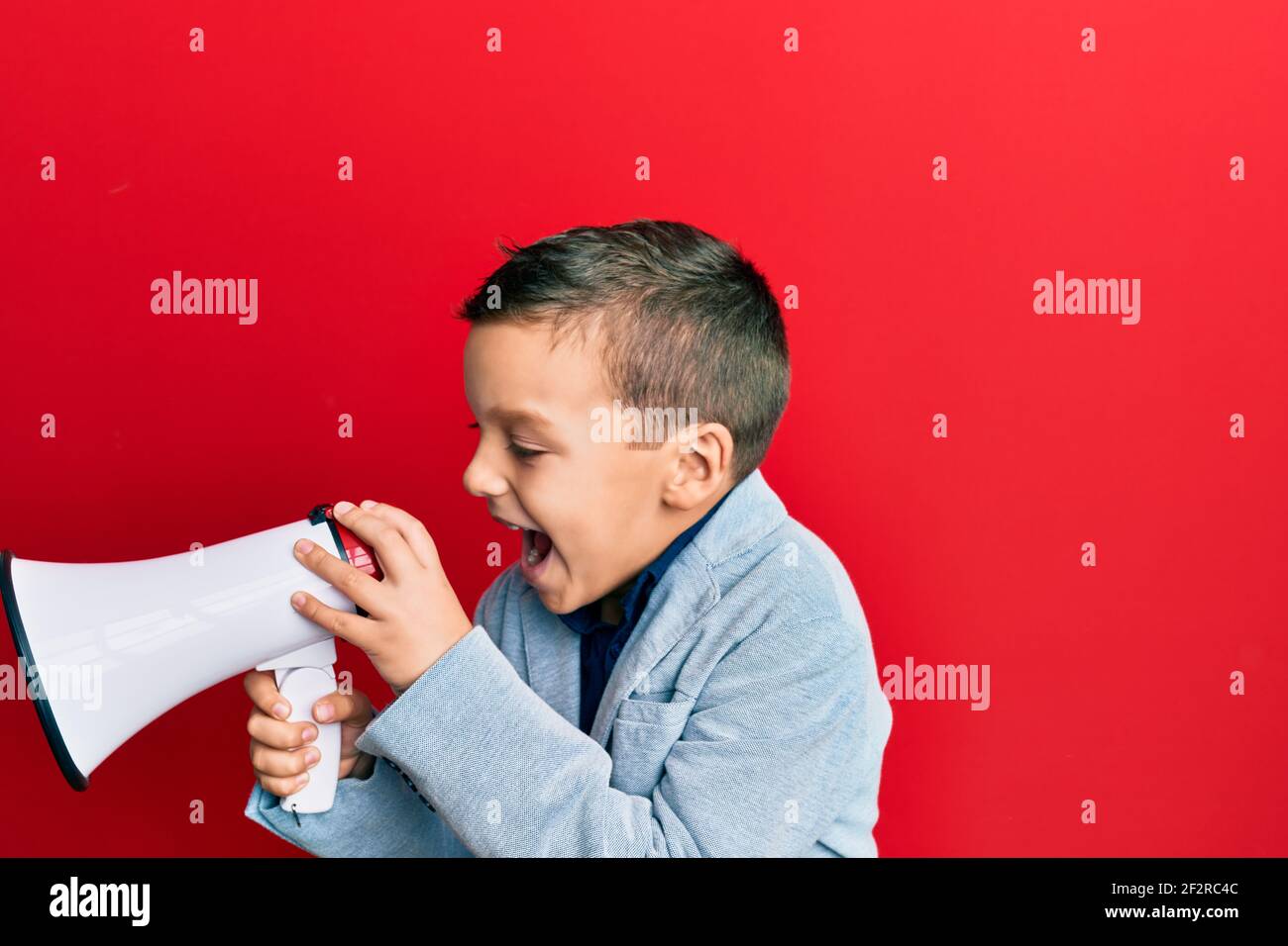 Adorable caucasian boy screaming using megaphone over isolated red ...