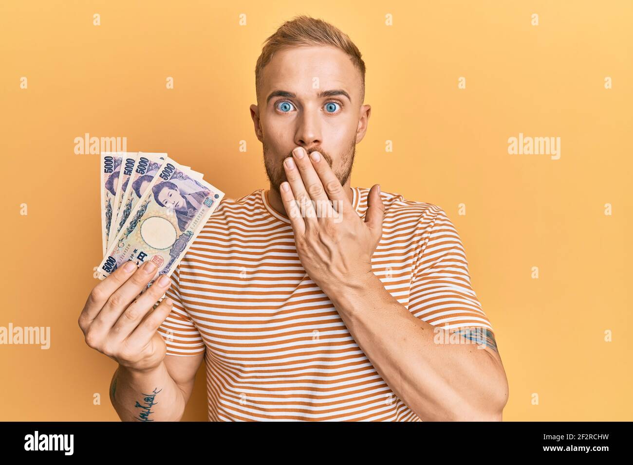 Young caucasian man holding japanese yen banknotes covering mouth with ...