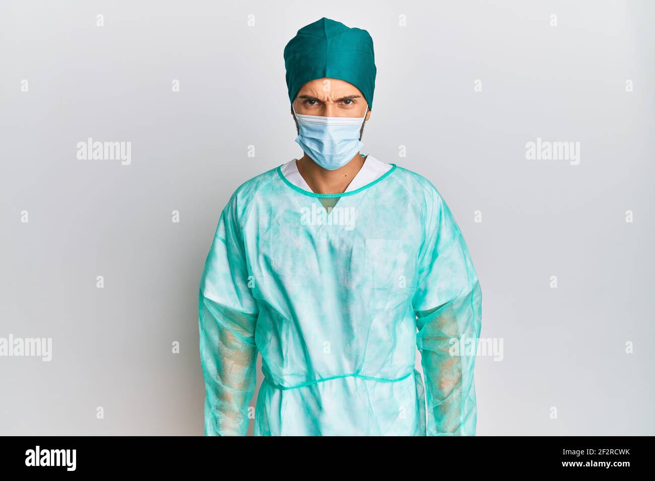 Young handsome man wearing surgeon uniform and medical mask skeptic and ...