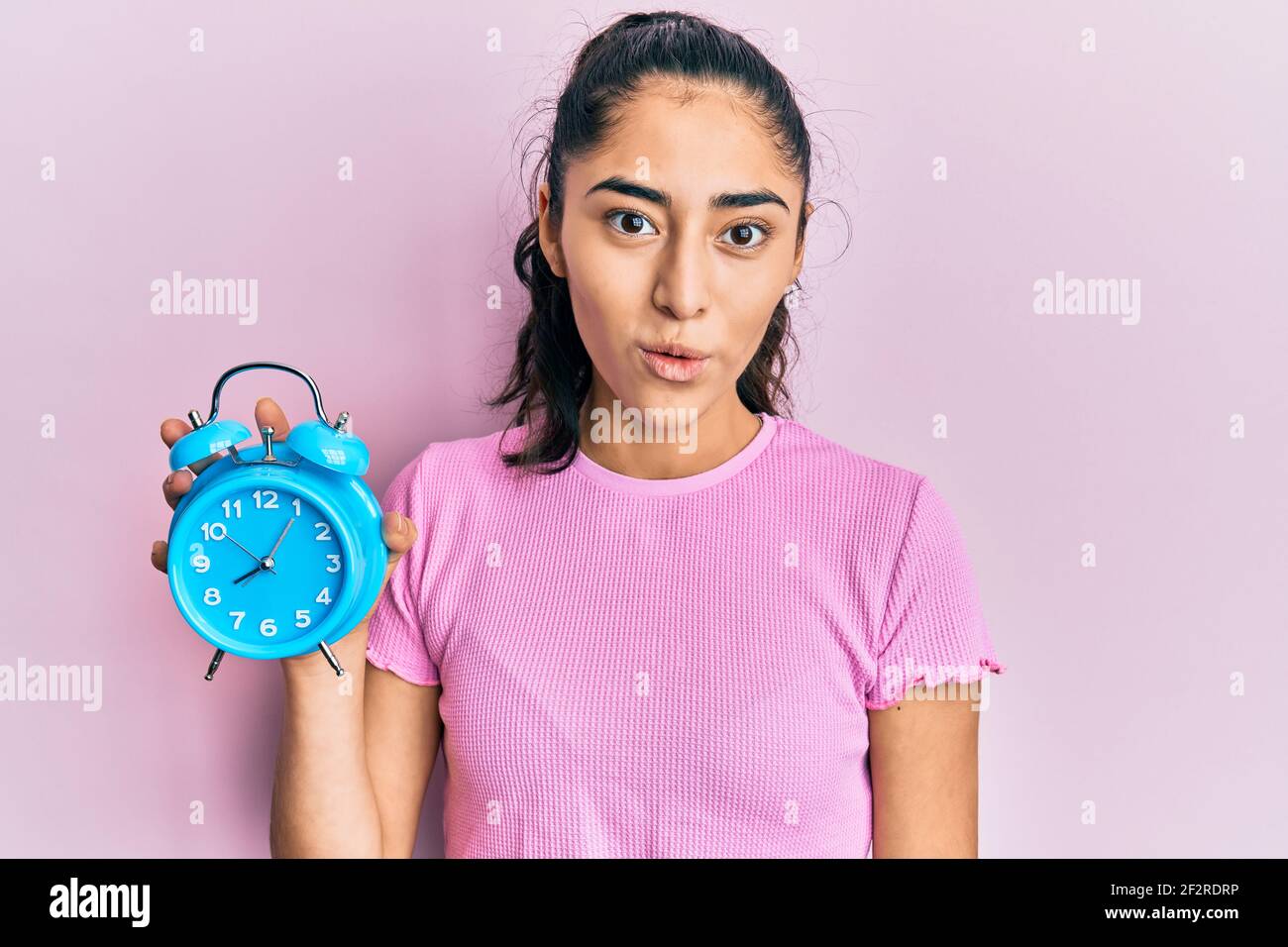 Hispanic teenager with dental braces holding alarm clock scared and ...