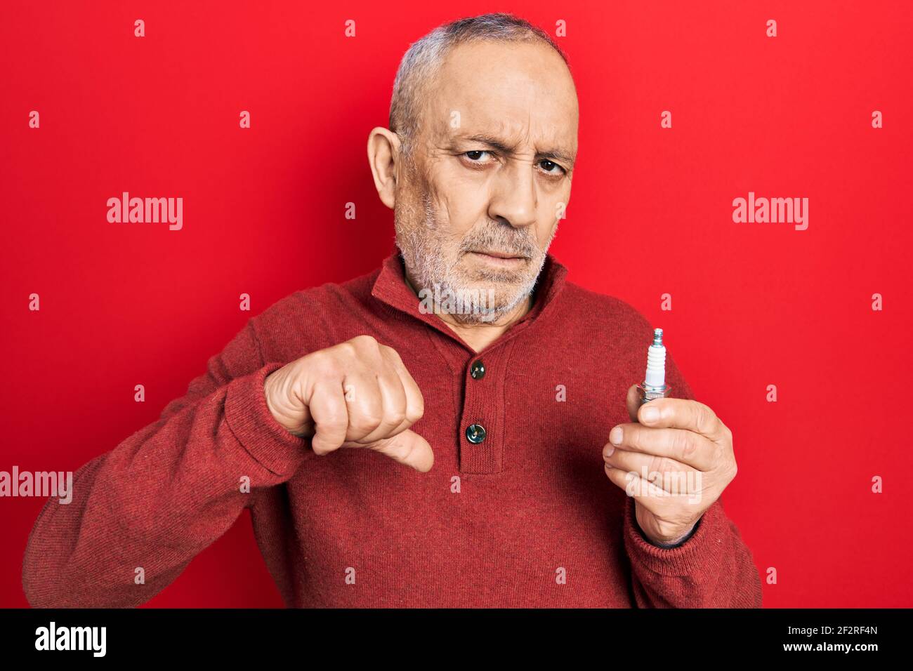 Handsome mature man holding spark plug with angry face, negative sign ...