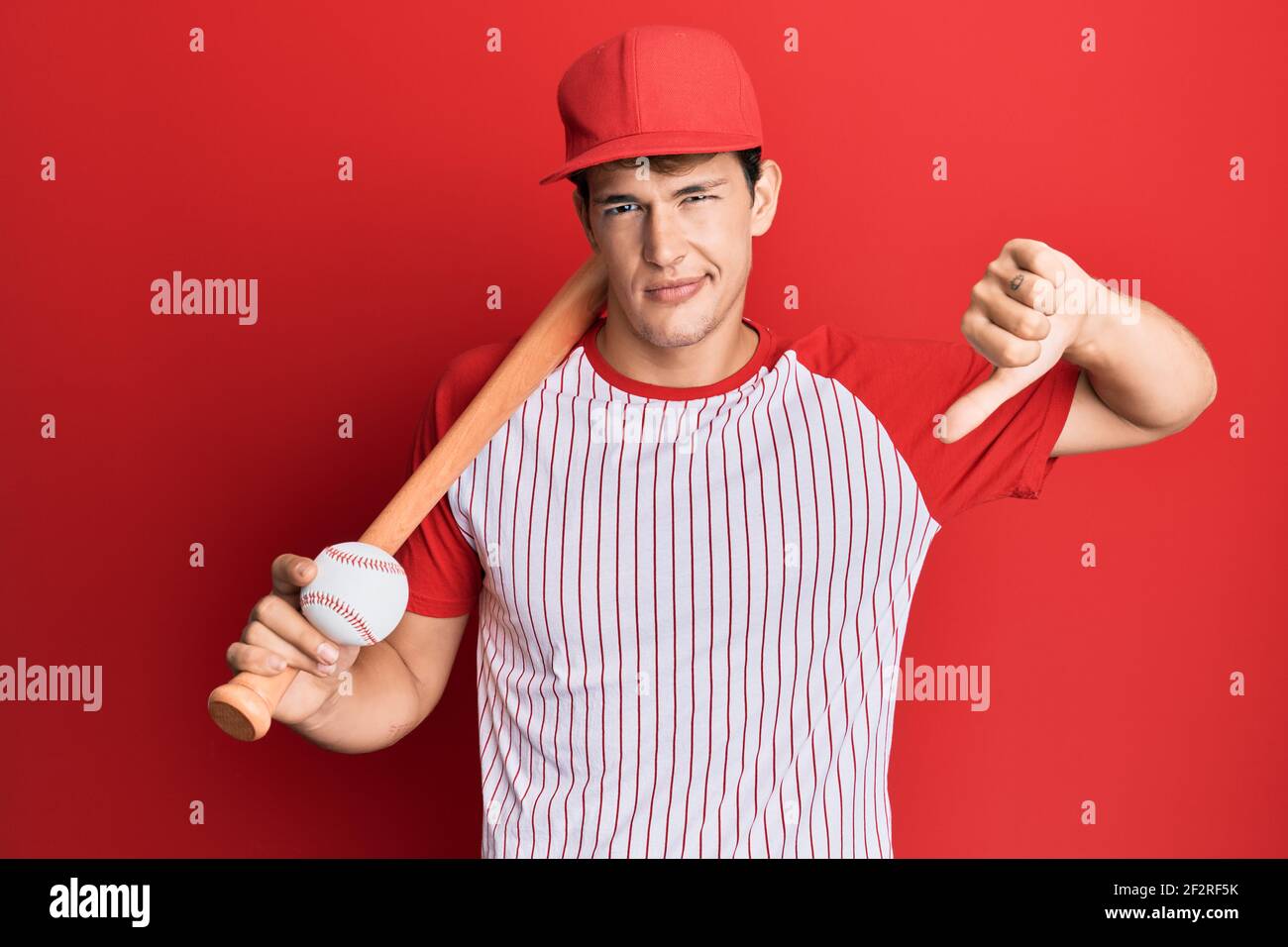 Handsome caucasian man playing baseball holding bat and ball with angry ...