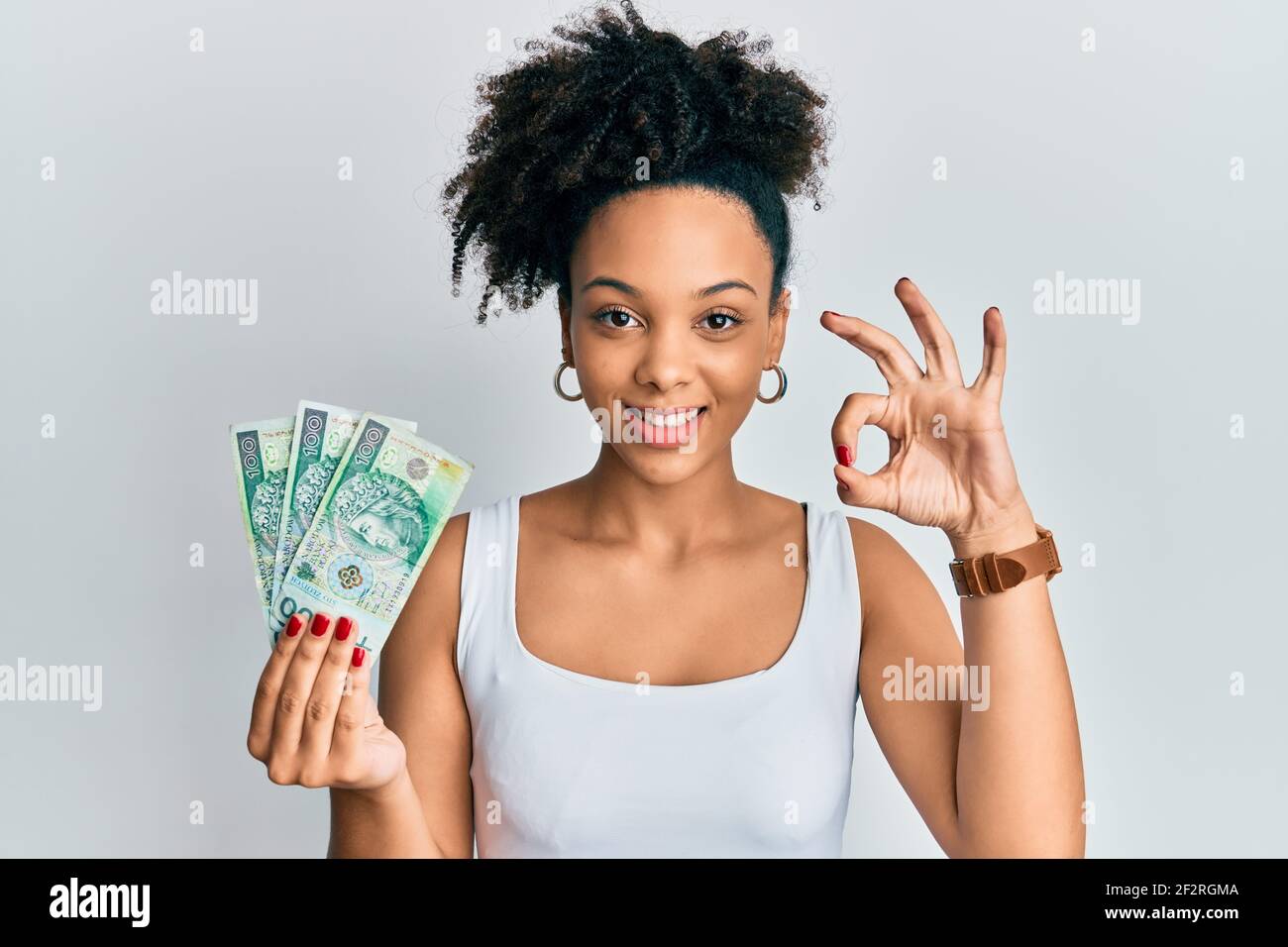 Young african american girl holding 100 polish zloty banknotes doing ok ...