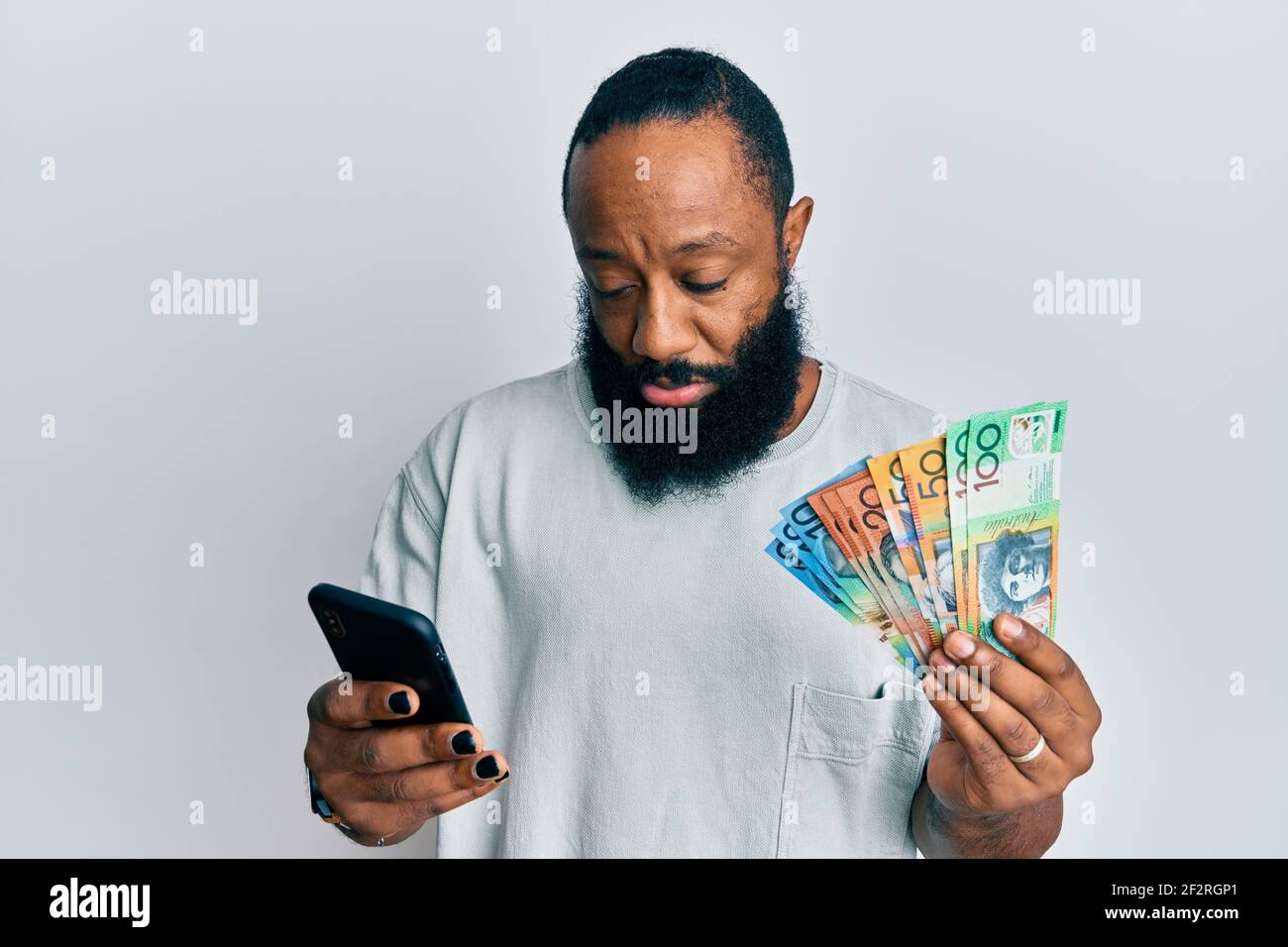 Young african american man using smartphone holding australia dollars ...