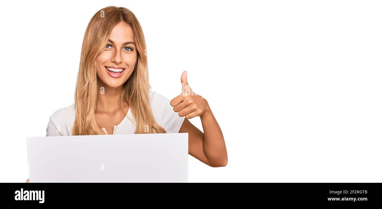 Beautiful blonde young woman holding blank empty banner smiling happy ...