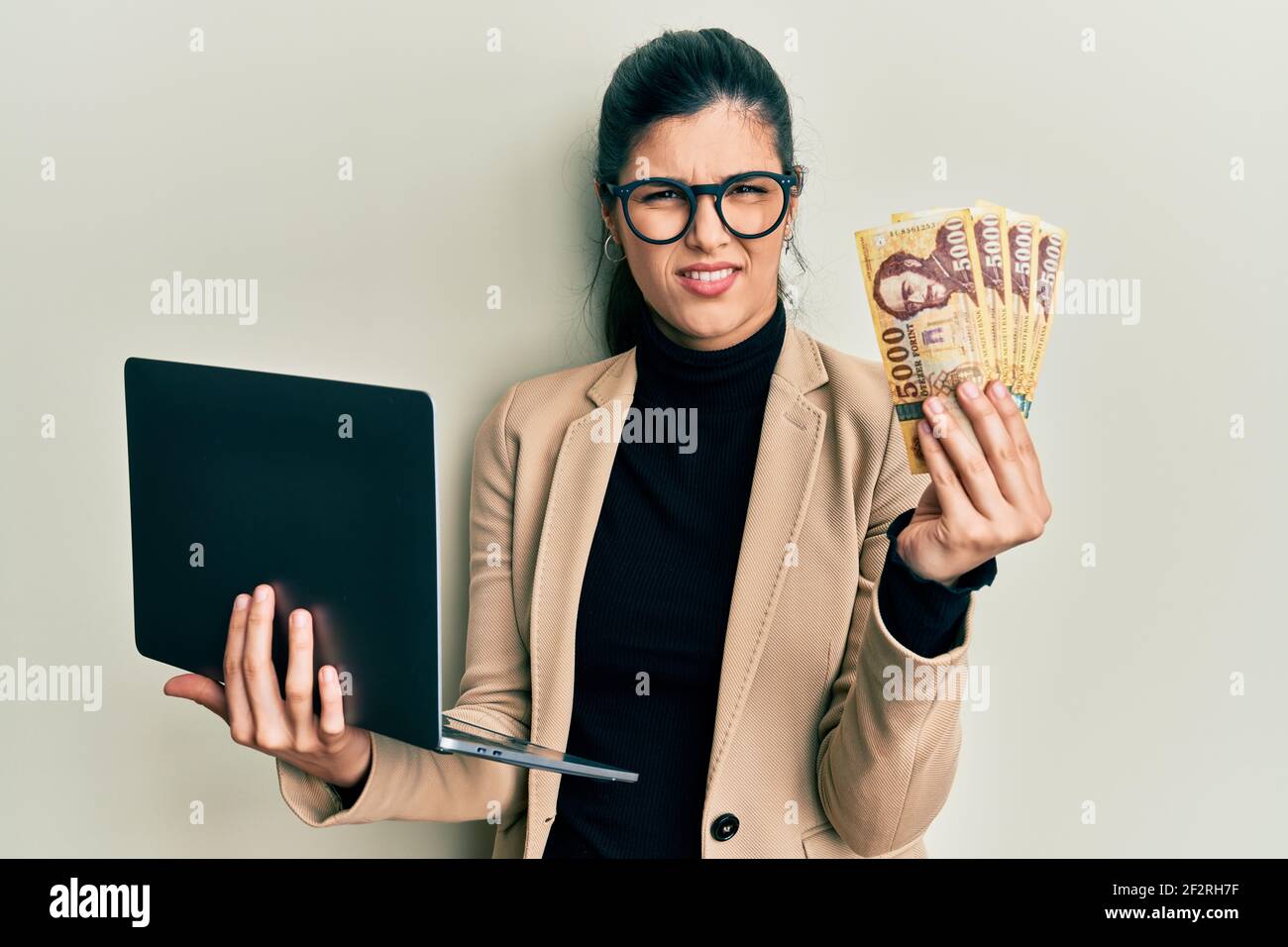 Young hispanic woman wearing business style holding laptop and ...