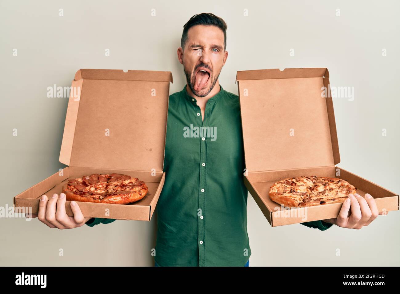 Handsome man with beard holding two italian pizzas sticking tongue out ...
