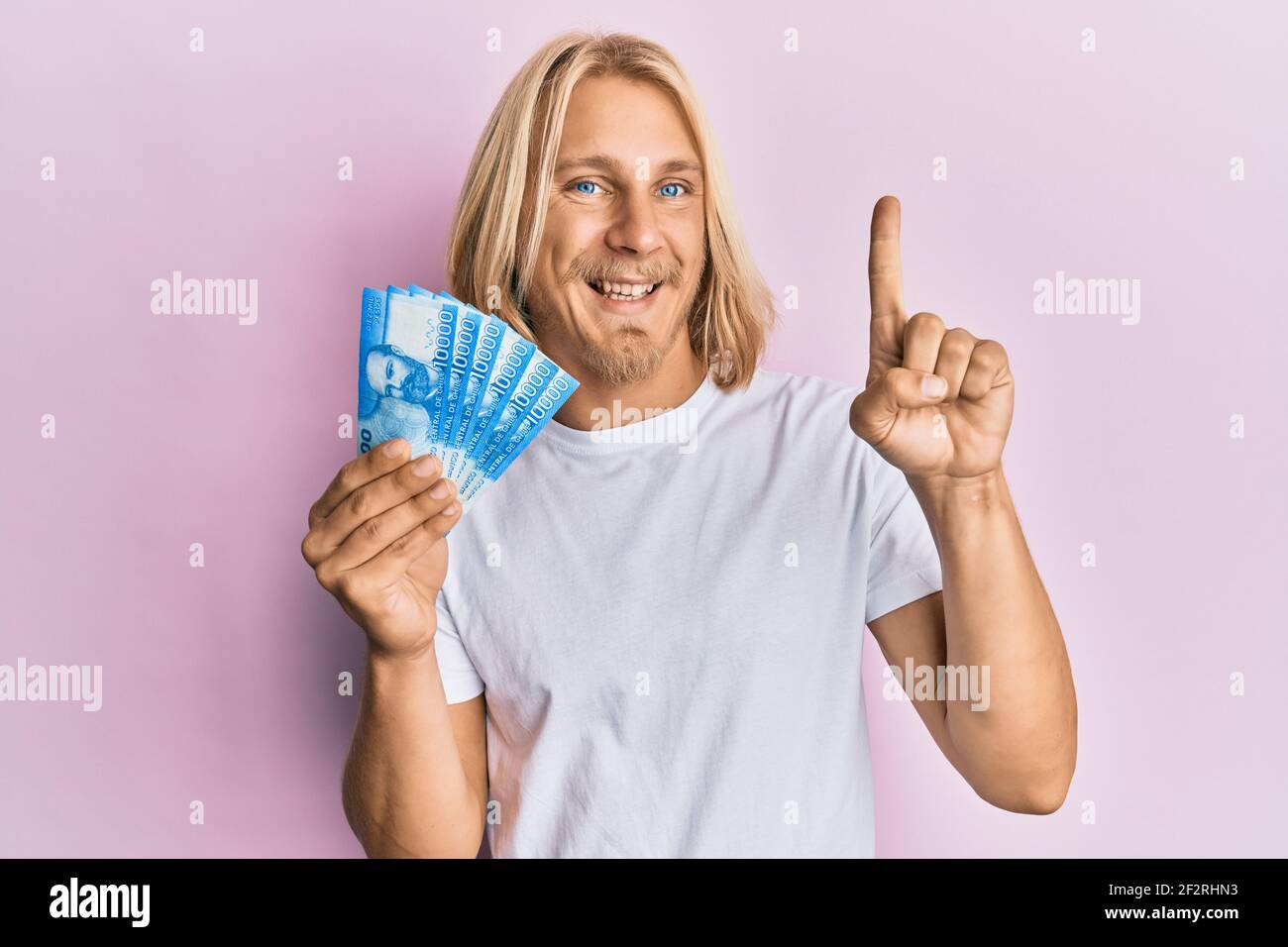 Caucasian young man with long hair holding 10000 chilean pesos smiling ...
