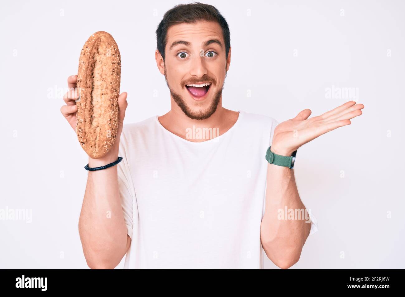 Young handsome man holding wholemeal bread celebrating achievement with ...