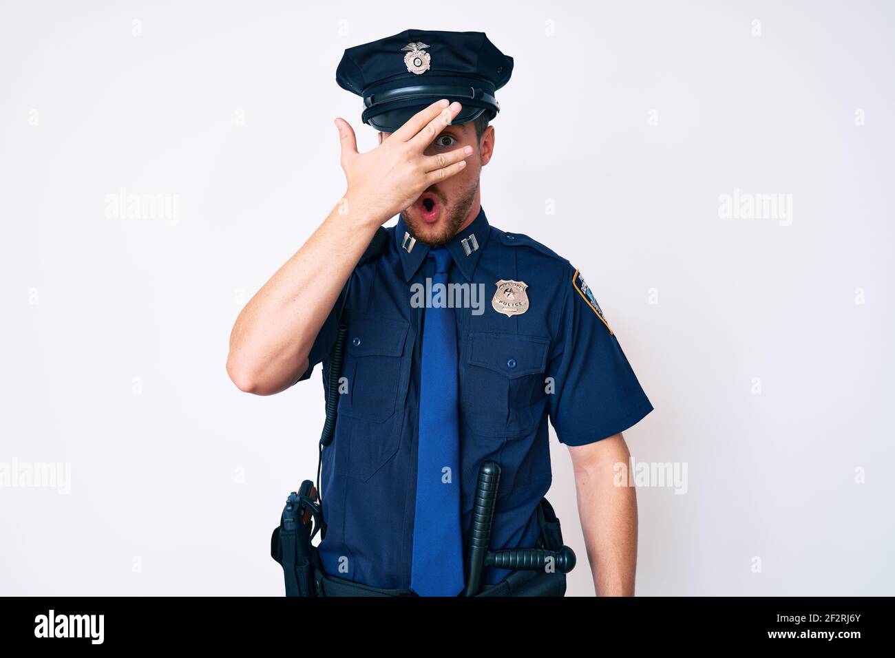Young caucasian man wearing police uniform peeking in shock covering ...