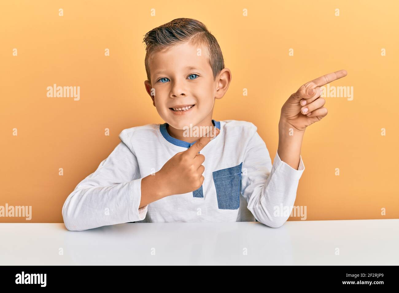 Adorable caucasian kid wearing casual clothes sitting on the table ...
