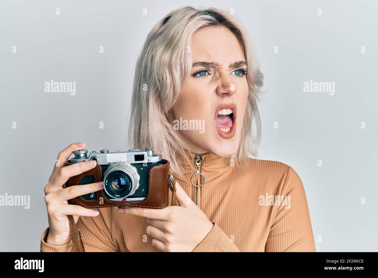Young blonde girl holding vintage camera angry and mad screaming ...