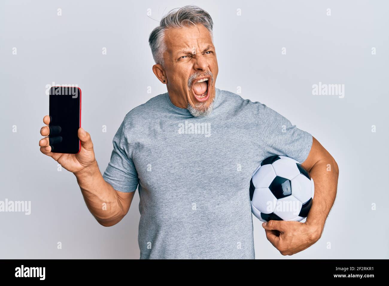 Middle age grey-haired man holding football ball showing smartphone ...