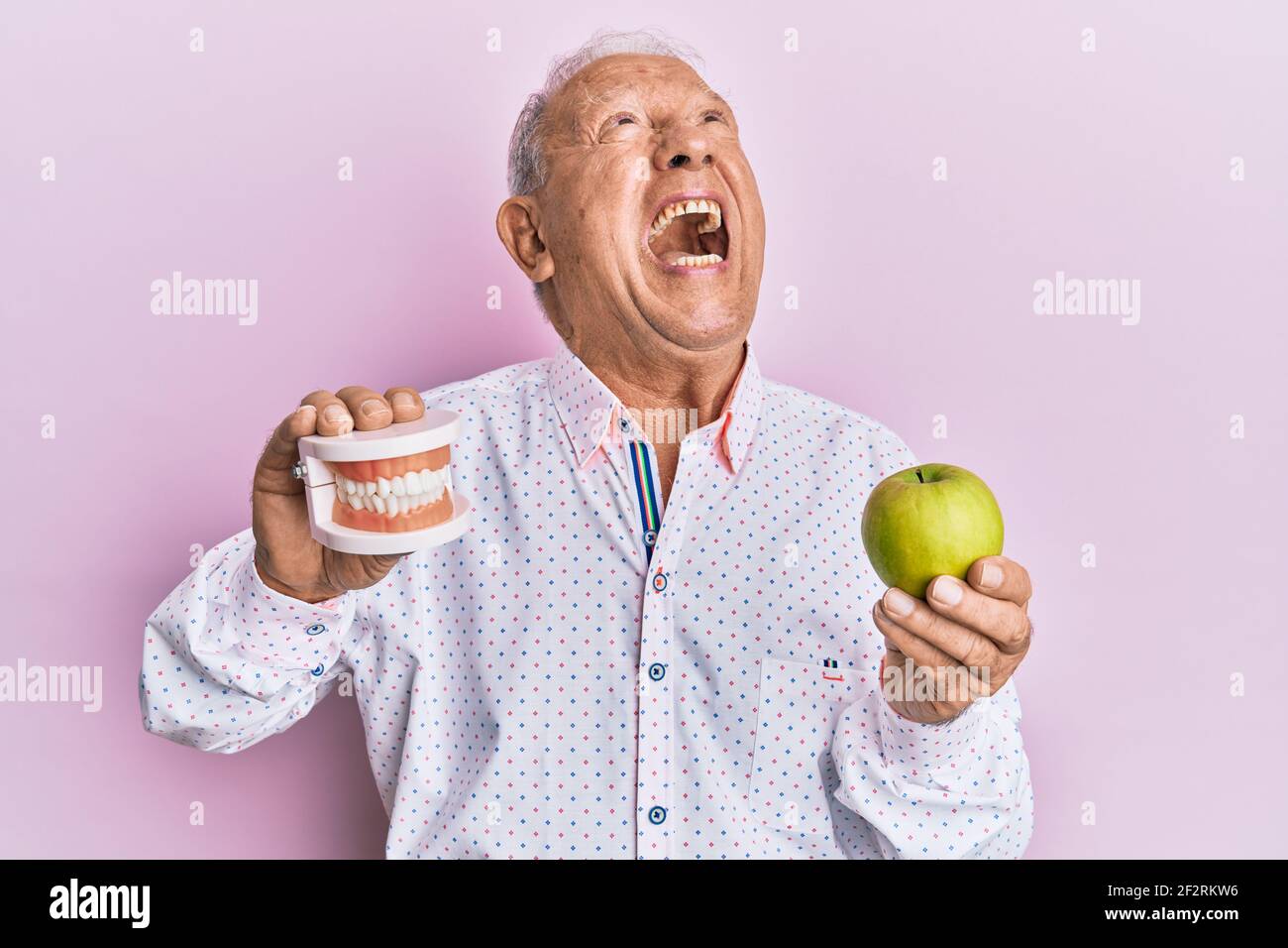 Senior caucasian man holding denture and green apple angry and mad ...