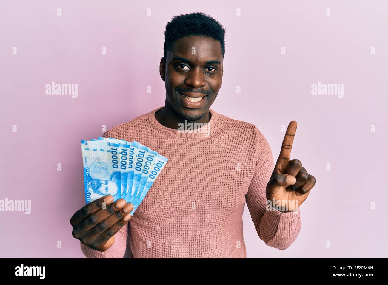 Handsome black man holding 10000 chilean pesos smiling with an idea or ...