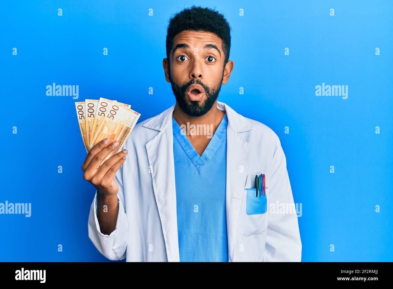 Handsome hispanic man with beard wearing medical uniform holding 500 ...