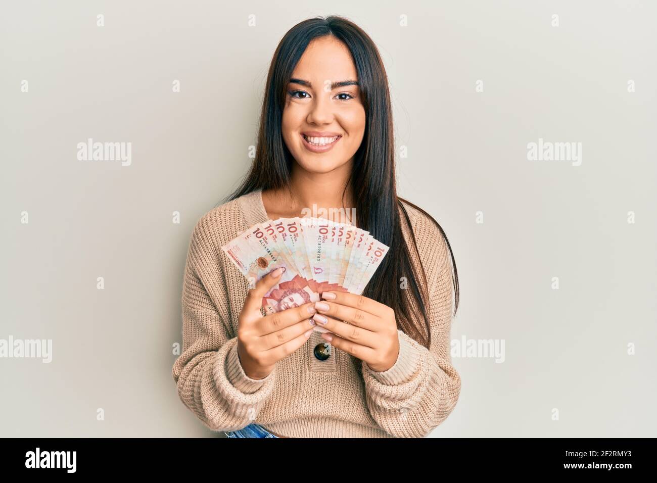 Young beautiful hispanic girl holding 10 colombian pesos banknotes ...