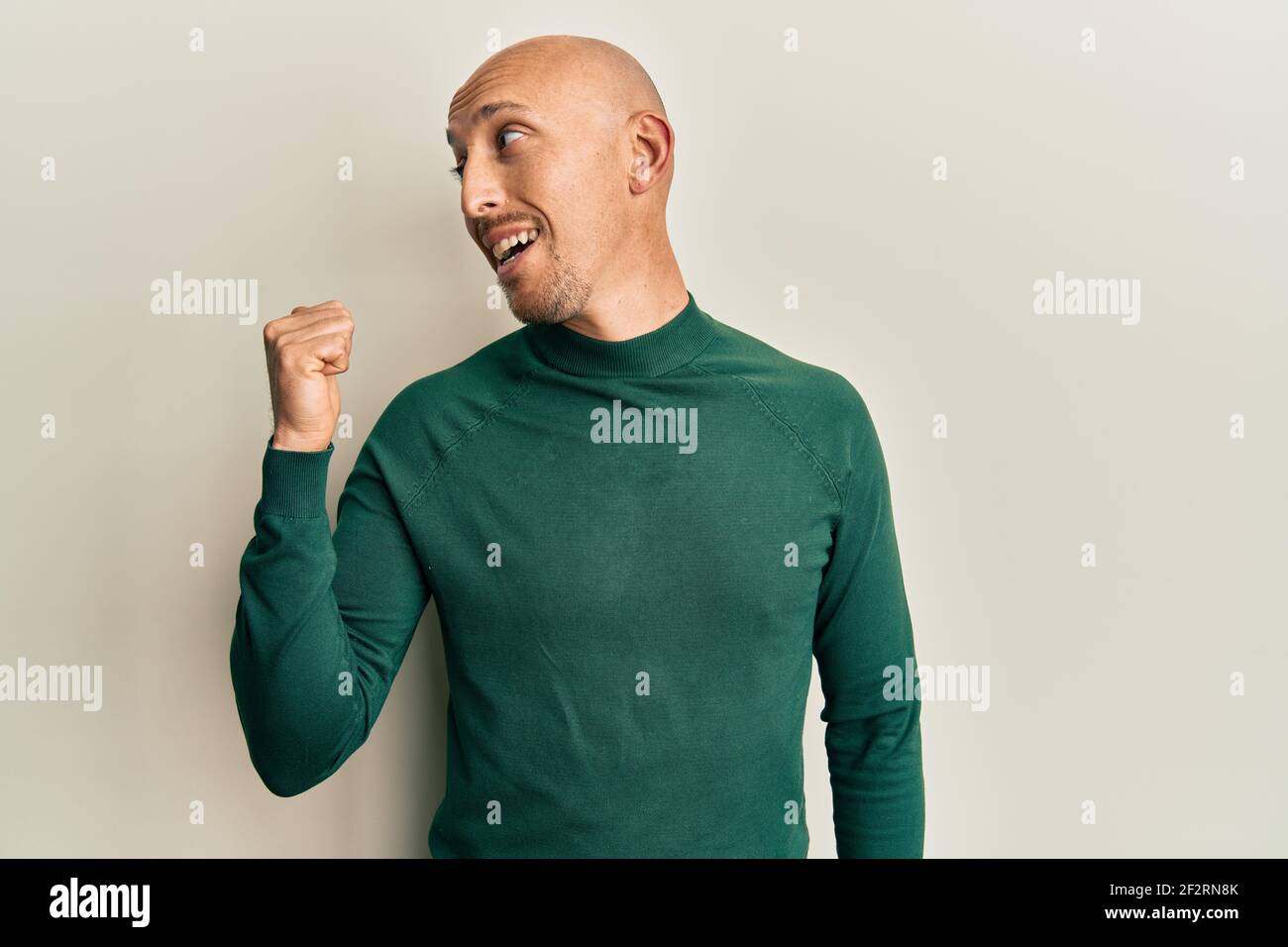 Bald man with beard wearing casual turtleneck sweater pointing thumb up ...