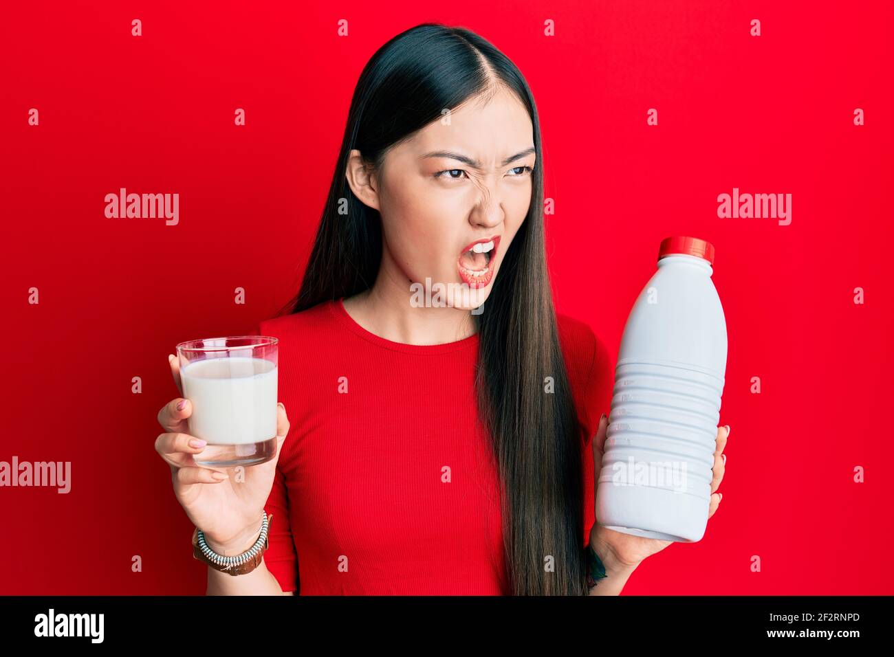 Young chinese woman drinking a glass of fresh milk angry and mad ...