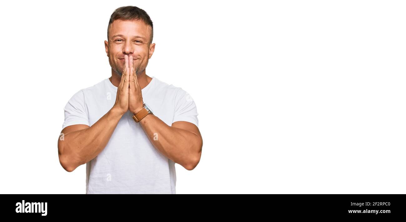 Handsome muscle man wearing casual white tshirt praying with hands ...