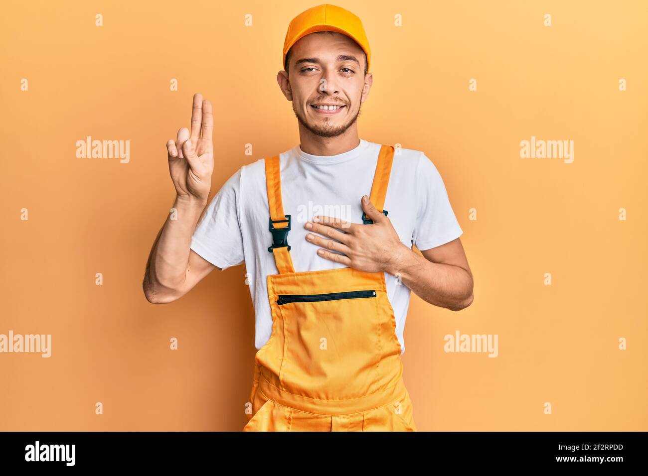 Hispanic young man wearing handyman uniform smiling swearing with hand ...