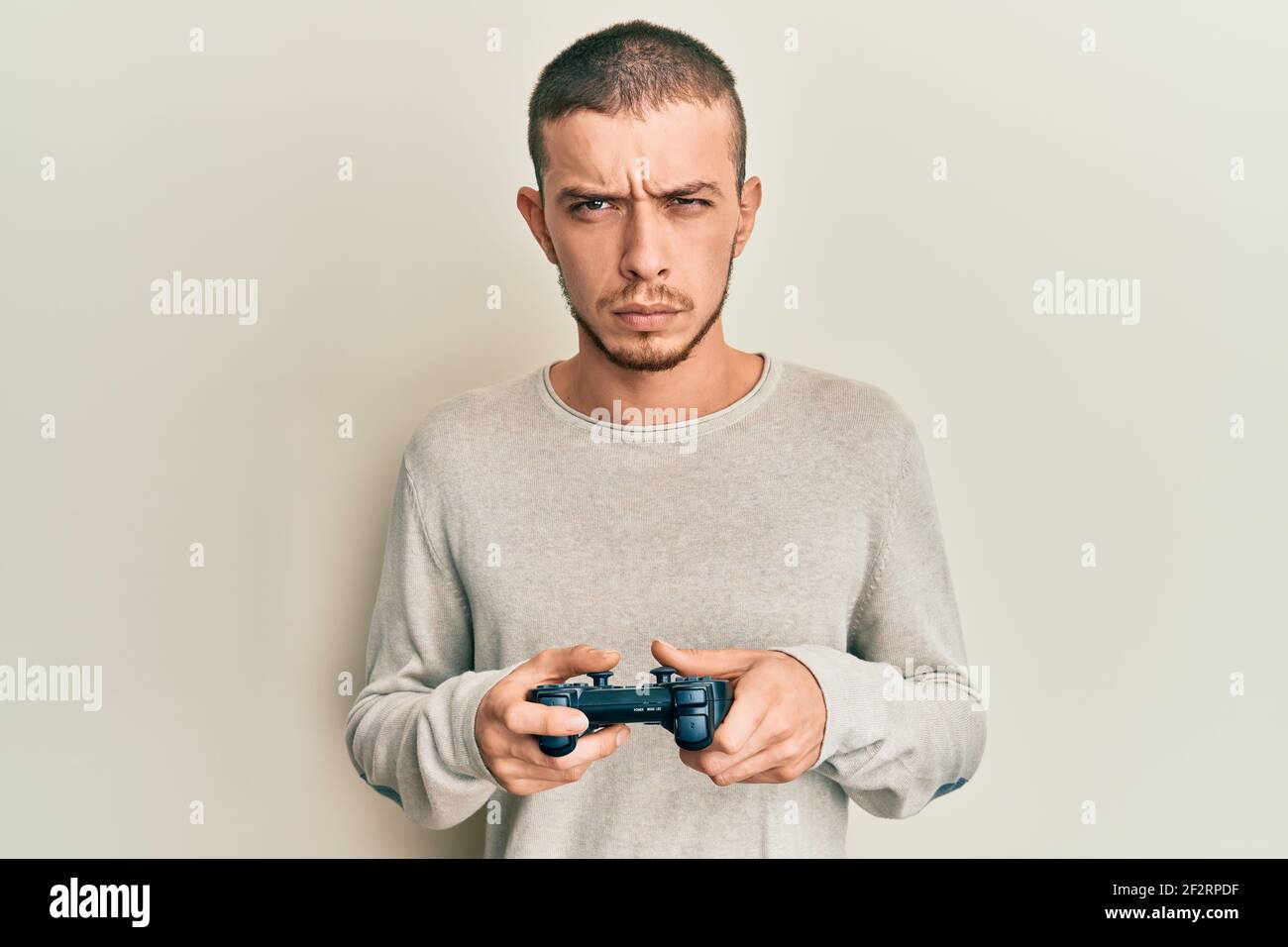 Hispanic young man playing video game holding controller skeptic and ...