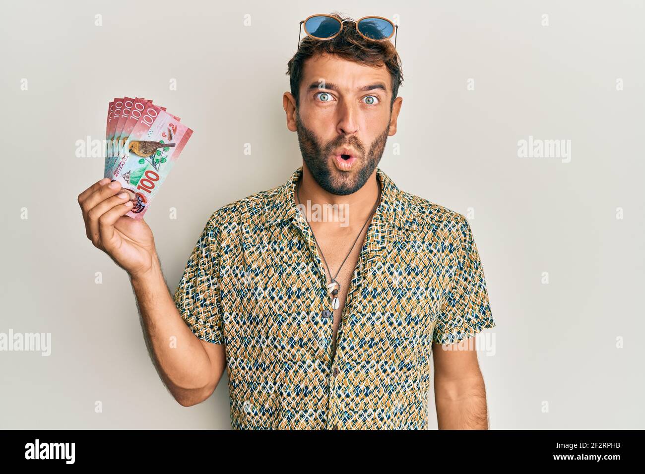 Handsome man with beard holding 100 new zealand dollars banknote scared ...