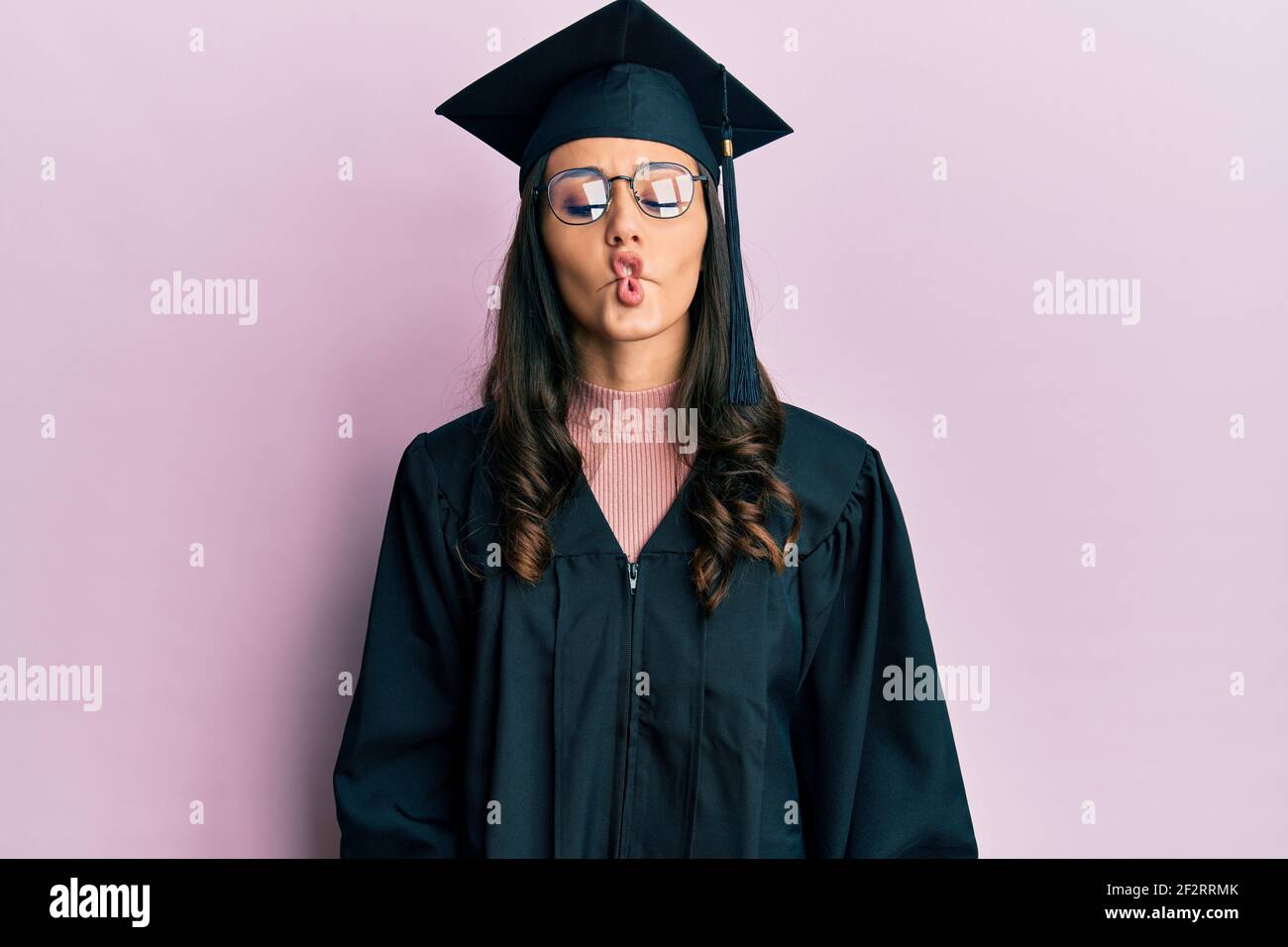 Young hispanic woman wearing graduation cap and ceremony robe making ...