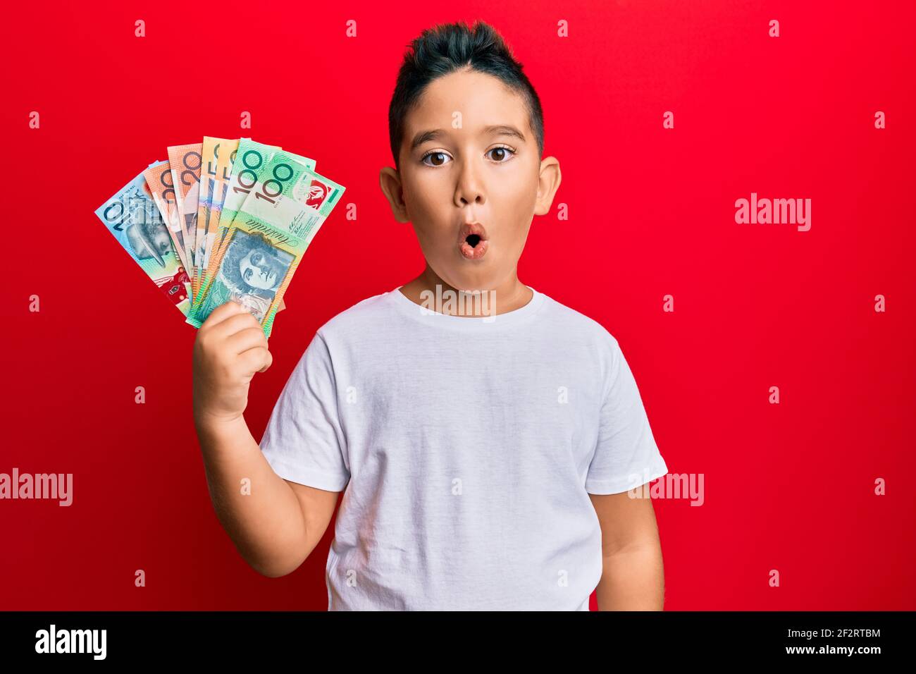 Little boy hispanic kid holding australian dollars scared and amazed ...