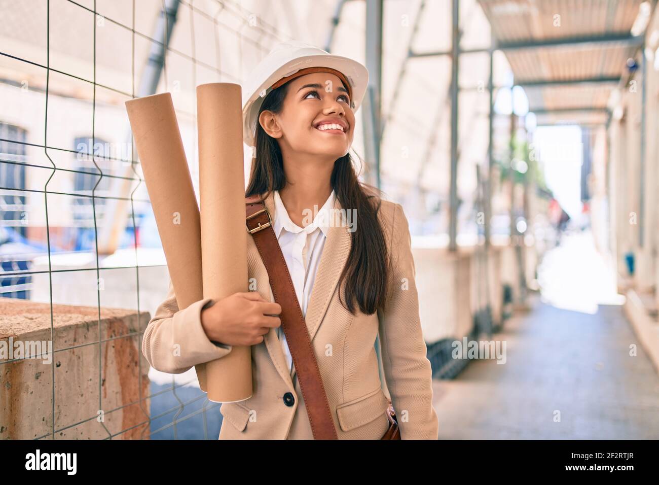 Young latin architect girl smiling happy holding blueprints standing at ...
