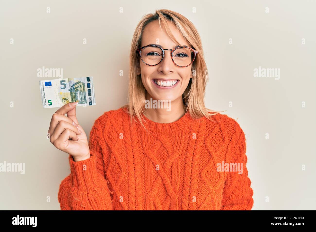 Beautiful blonde woman holding 5 euro banknote looking positive and ...
