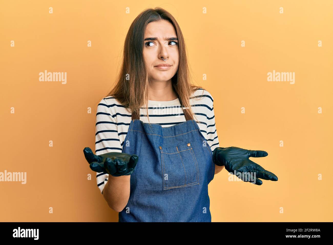 Young hispanic woman wearing barber apron clueless and confused ...