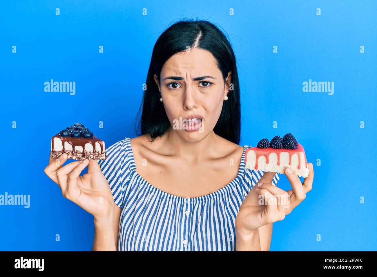 Beautiful young woman holding cake slices in shock face, looking ...