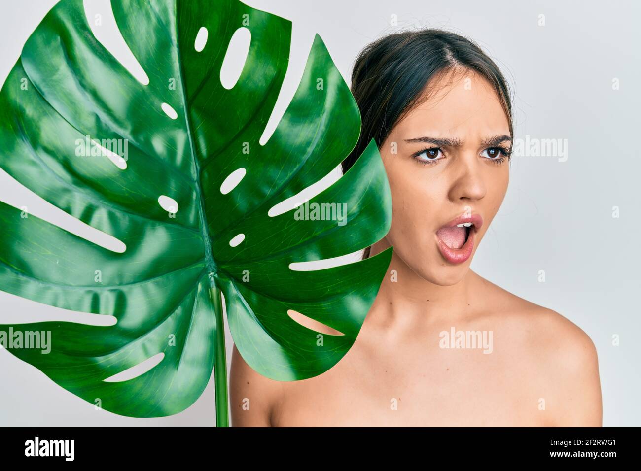 Young brunette woman holding green plant leaf close to beautiful face ...