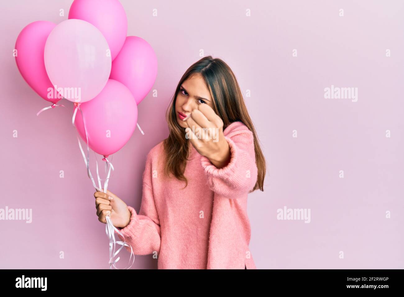 Young brunette woman holding pink balloons annoyed and frustrated ...