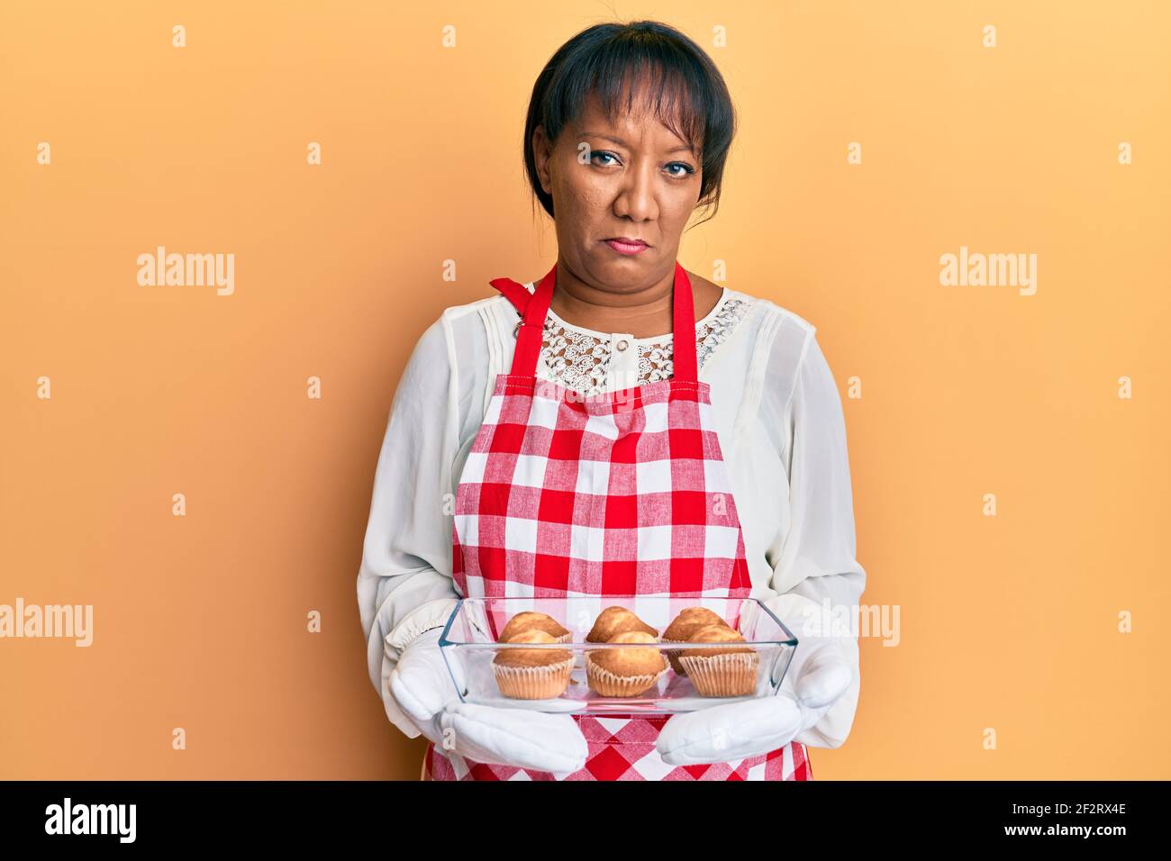 Middle age african american woman wearing baker apron holding muffins ...