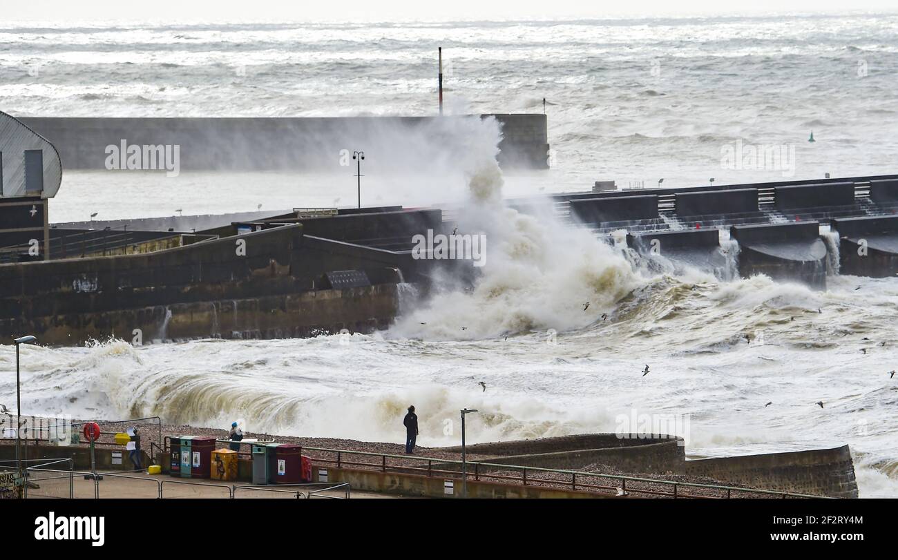 Brighton UK 13th March 2021 - People on the beach watch as waves crash ...