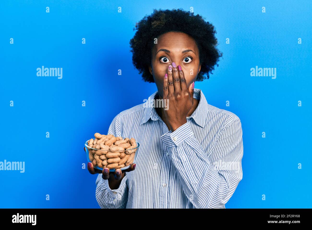 Young african american woman holding peanuts covering mouth with hand ...
